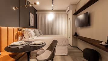 Quarto de hotel moderno com uma cama, uma mesa de jantar com cadeiras, um sofá, uma TV na parede e um ar condicionado.
