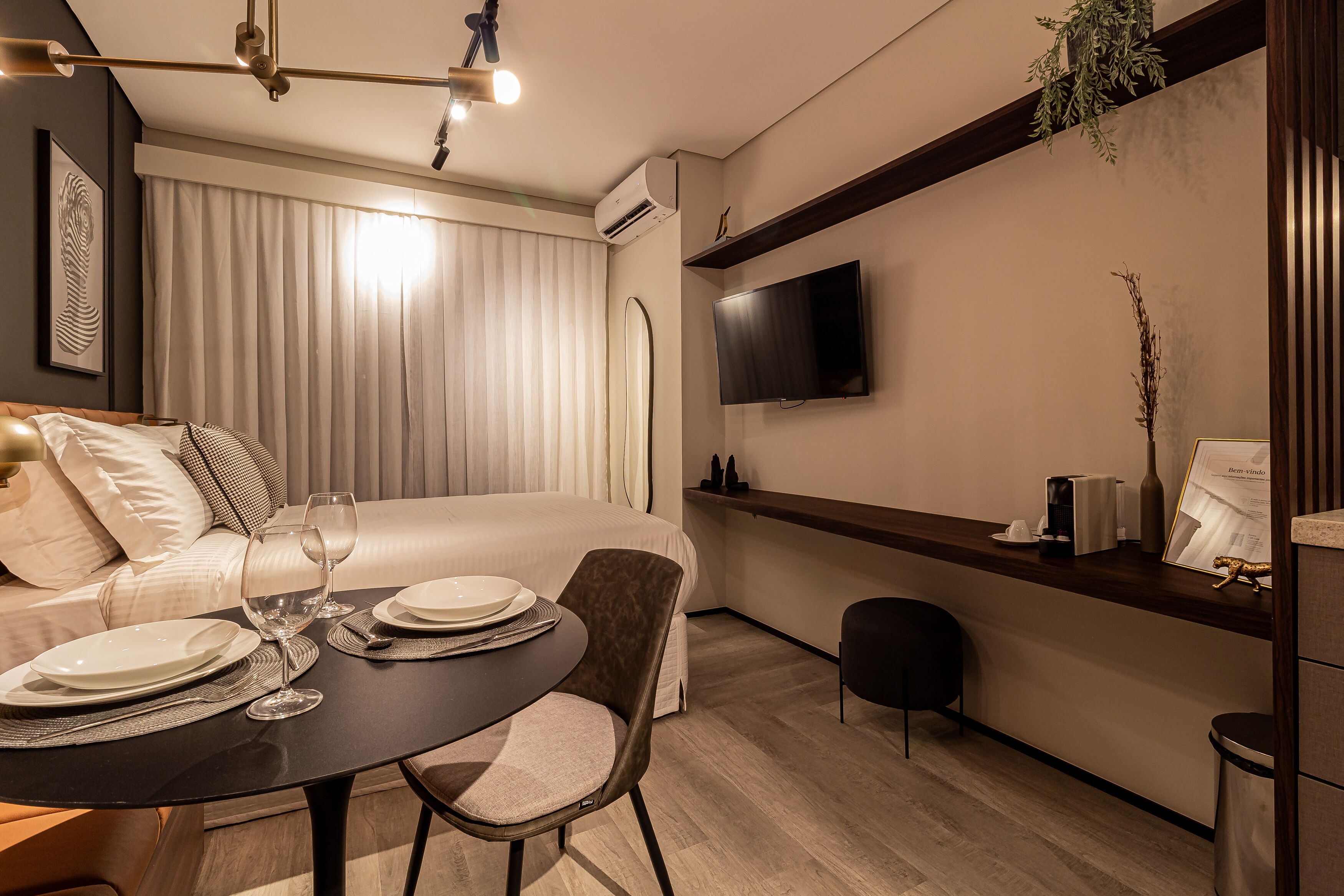 Quarto de hotel moderno com uma cama, mesa de cabeceira e televisão fixada na parede.