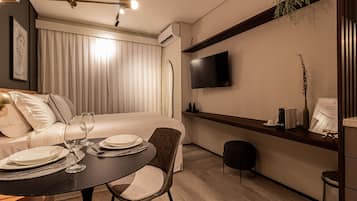 Quarto de hotel moderno com uma cama, mesa de cabeceira e televisão fixada na parede.