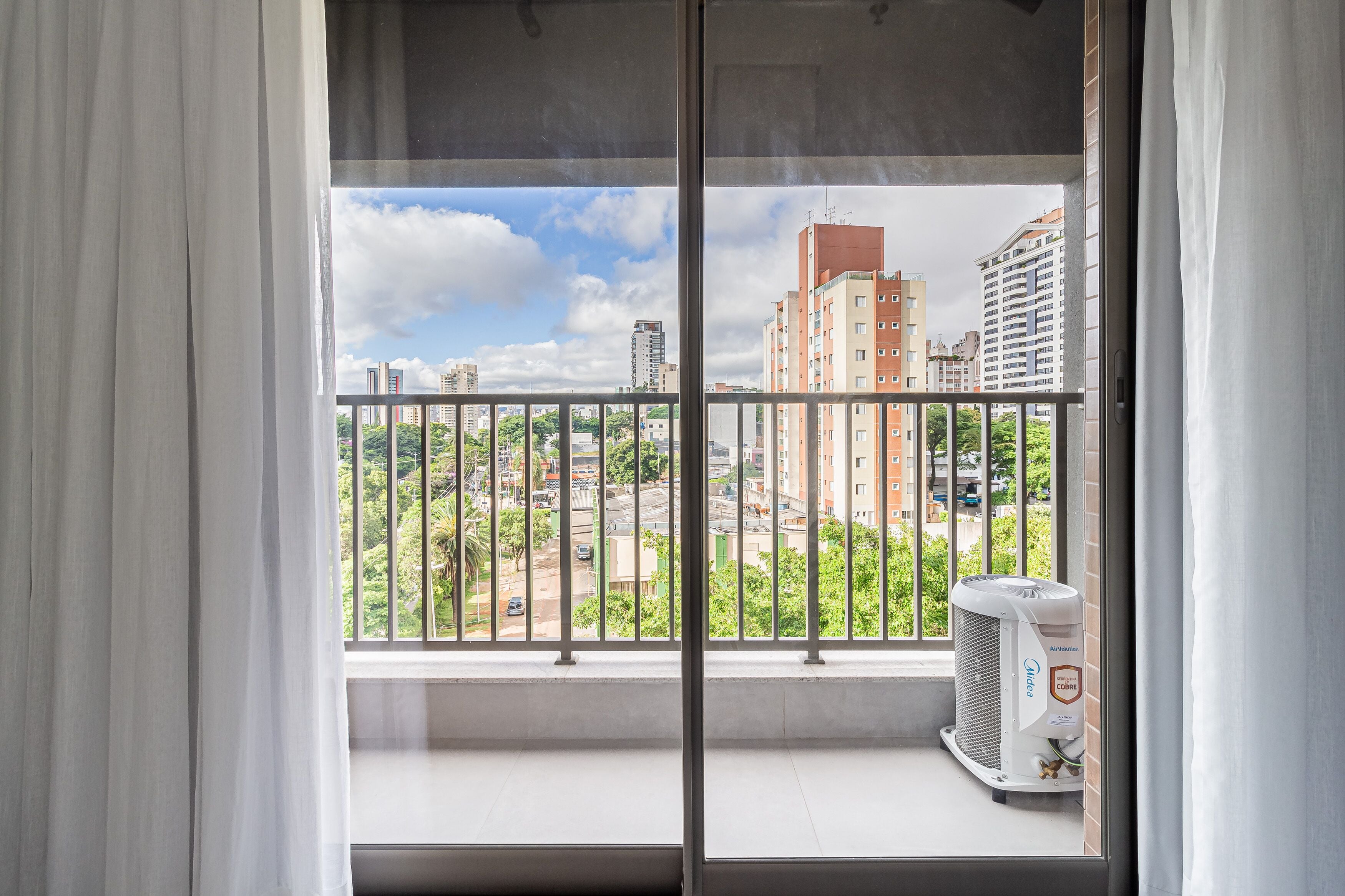 Uma varanda com vista para a cidade, uma janela com cortina e um ar condicionado portátil.