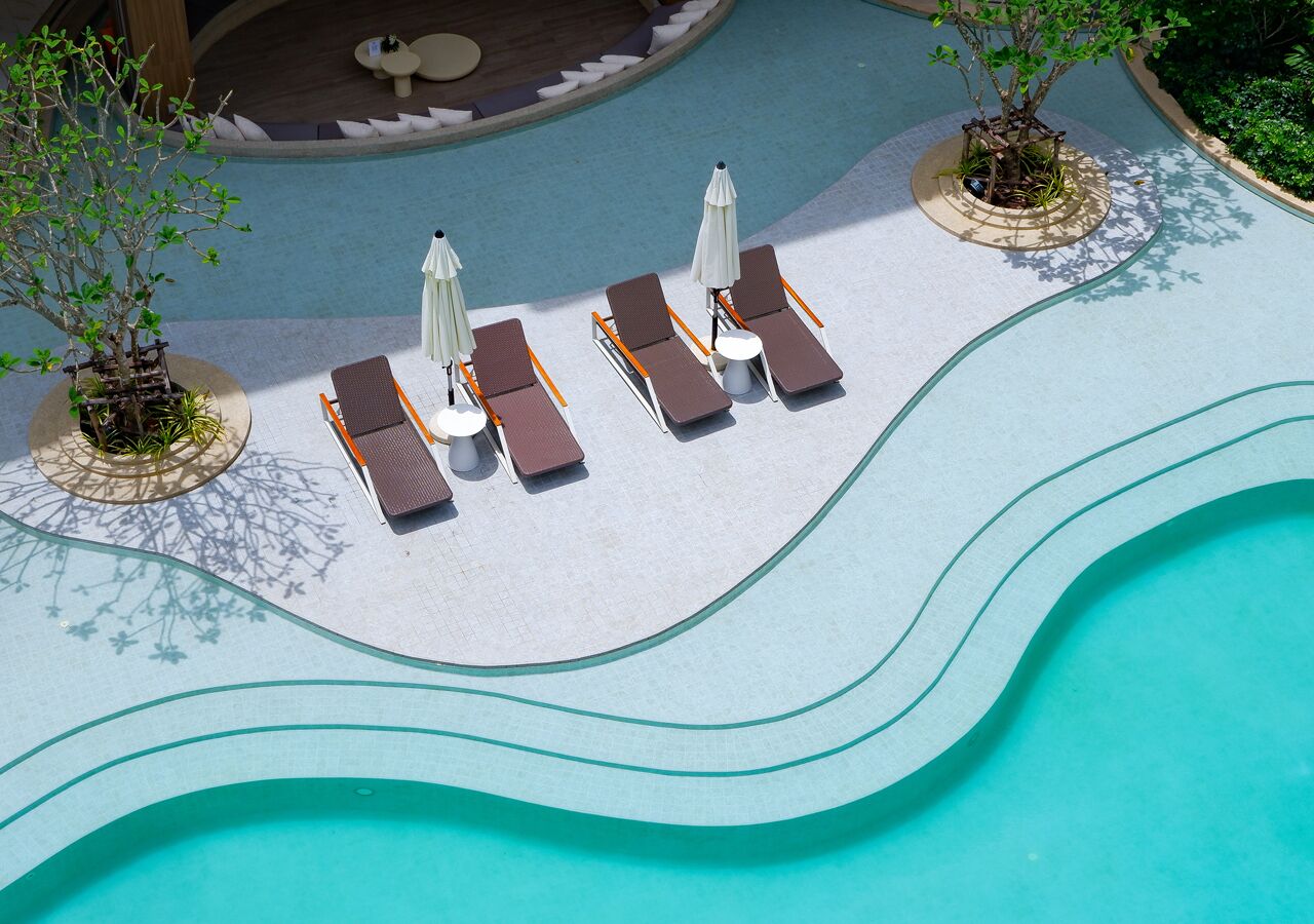 Uma área de piscina com espreguiçadeiras e guarda-sóis, delimitada por uma borda de piscina ondulada.