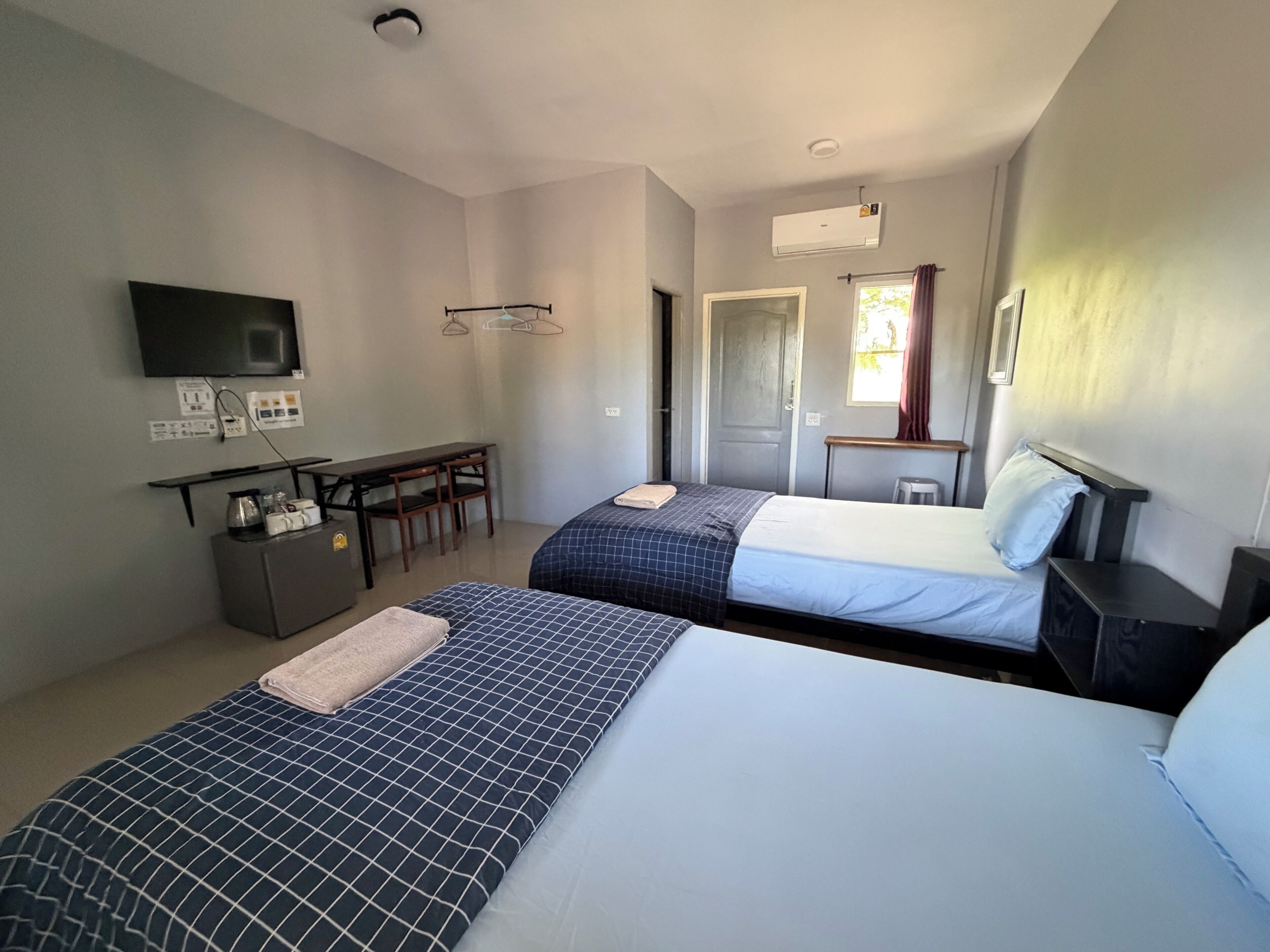 Quarto com duas camas, uma escrivaninha com cadeiras, televisão e ar condicionado.