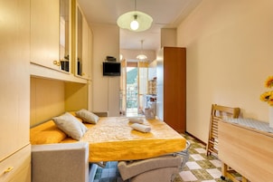 Quarto com cama, escrivaninha, cadeira e televisão.