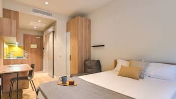 Quarto de hotel moderno com cama, escrivaninha e cadeira, uma pequena mesa com uma chávena e outra cadeira.