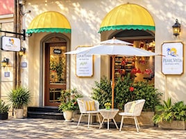 Área externa com assentos, cadeiras, uma mesa, placa indicando 'Pearl Vista Boutique Hotel' e sinalização de 'Courtyard' para restaurante, café no jardim e bar de cocktails.