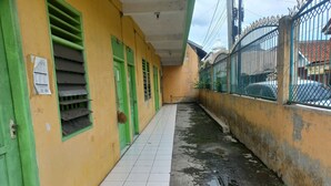 Um corredor estreito com paredes amarelas e portas verdes, que leva a uma área murada.