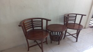 Conjunto de três cadeiras de madeira e uma pequena mesa redonda, com uma parede lisa ao fundo.