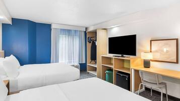 Quarto de hotel com uma cama, escrivaninha com luminária, televisão e armário.