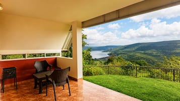 Varanda com vista para um lago e montanhas, mobiliada com cadeiras e uma mesa.
