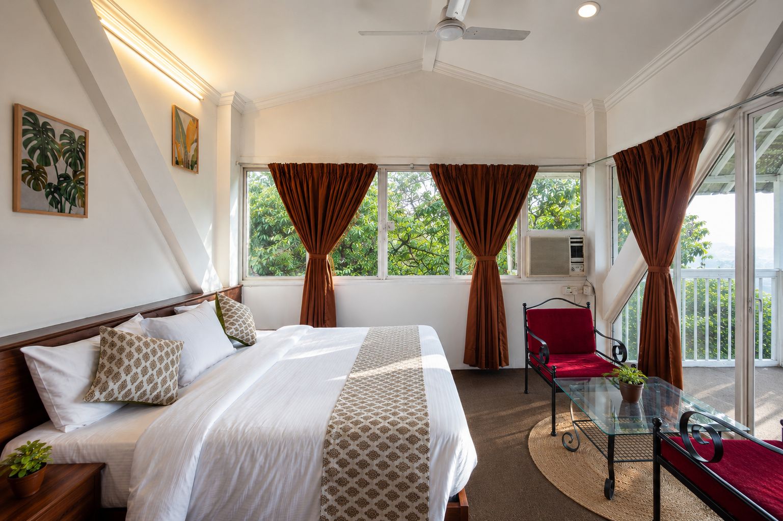 Quarto de hotel com cama, mesa de vidro, cadeira vermelha e varanda com cortinas.