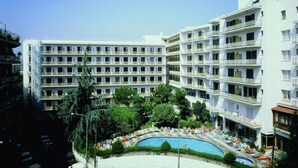Um hotel com vários andares e piscina, rodeado por vegetação.