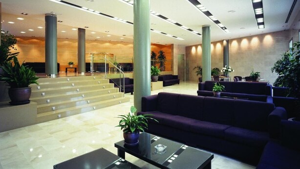 Um hall amplo com balcão de recepção, área de estar e escadaria para os andares superiores.