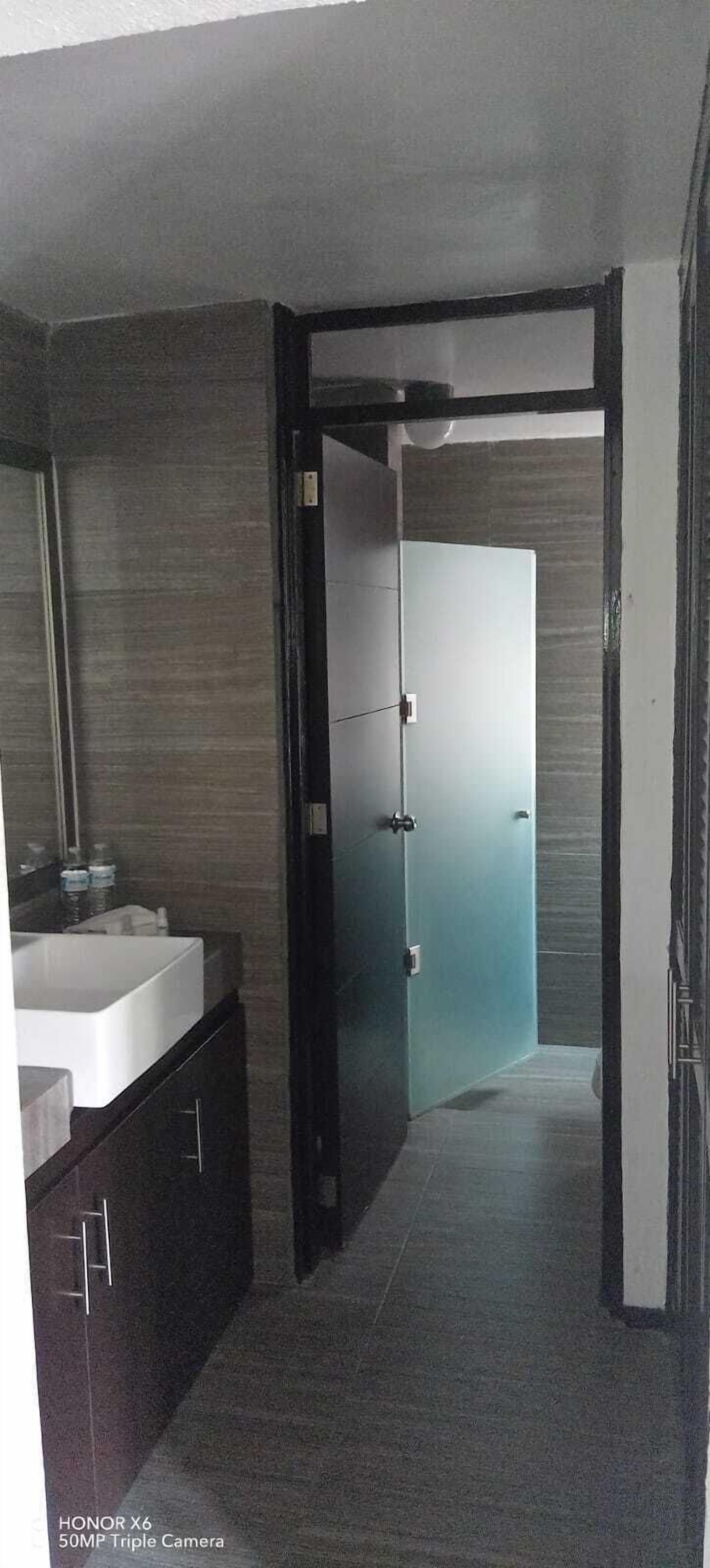 Uma casa de banho moderna com um espelho grande, uma sanita branca e armários escuros.