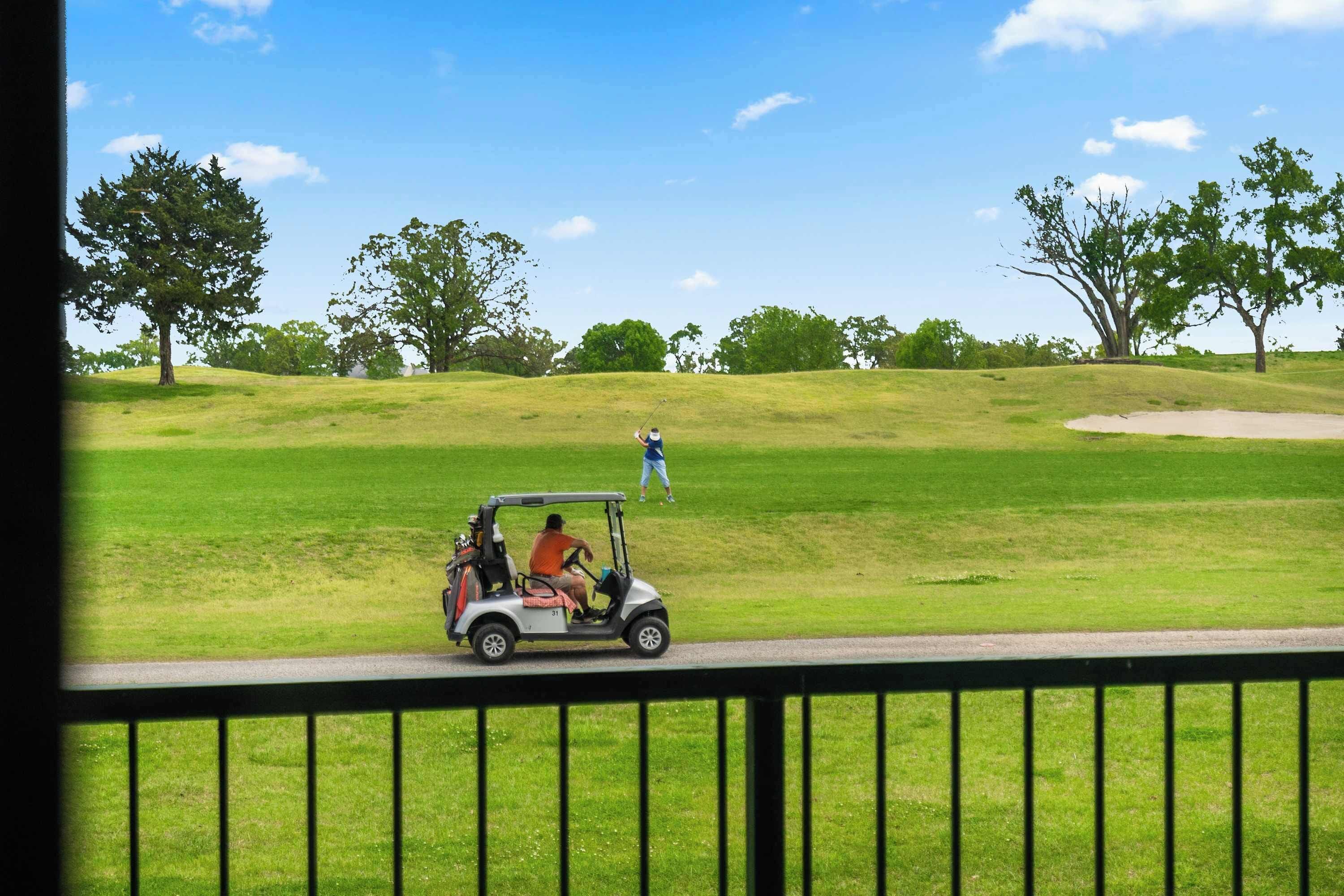 Um campo de golfe com um carrinho de golfe e uma pessoa caminhando.