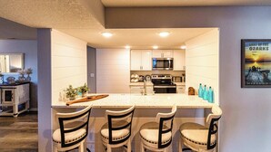 Uma cozinha moderna com armários brancos, uma ilha central com banquetas e um micro-ondas sobre a ilha.