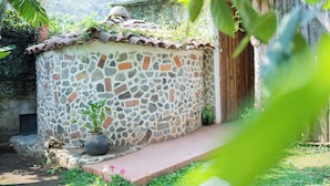 Um edifício de pedra com telhado de telhas, uma planta em vaso e um pequeno jardim.