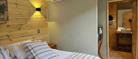 Quarto com cama, mesa de cabeceira, ar condicionado fixado na parede e cabeceira de madeira.