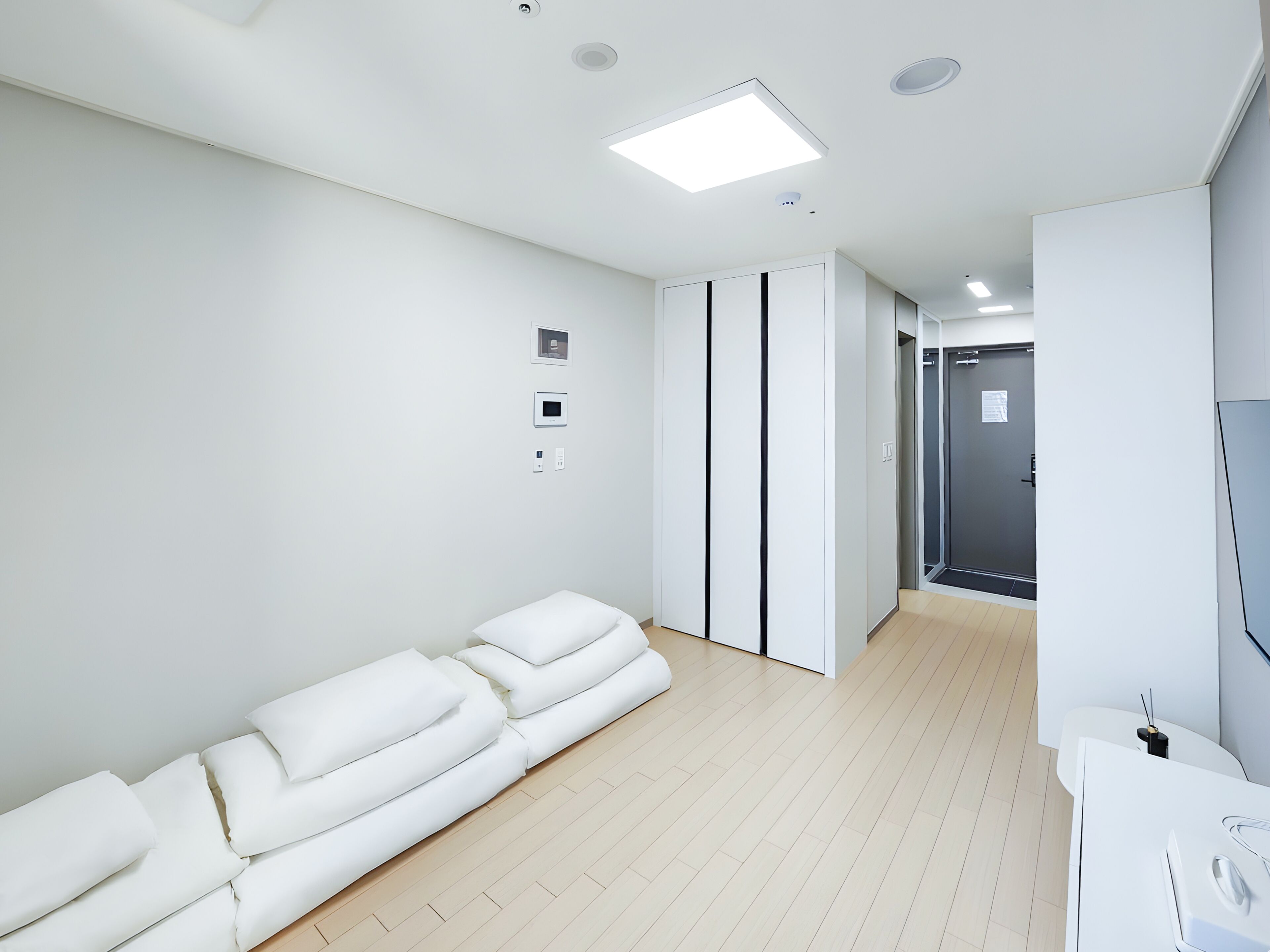 Quarto moderno e minimalista com sofá branco, televisão de tela plana e piso de madeira.