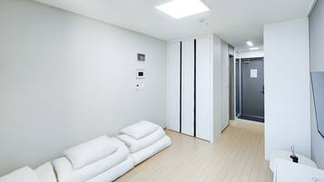 Quarto moderno e minimalista com sofá branco, televisão de tela plana e piso de madeira.