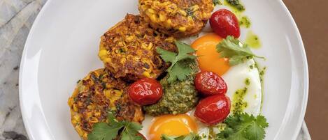 Um prato branco com três hambúrgueres dourados, tomates cereja, um ovo pochê e um molho verde sobre uma superfície de mármore.