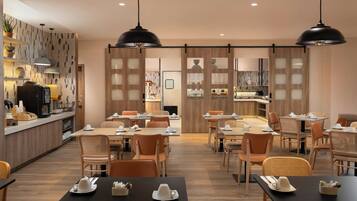 Um restaurante moderno com piso de madeira, luminárias pendentes pretas e diversas opções de assentos, incluindo mesas e cadeiras.