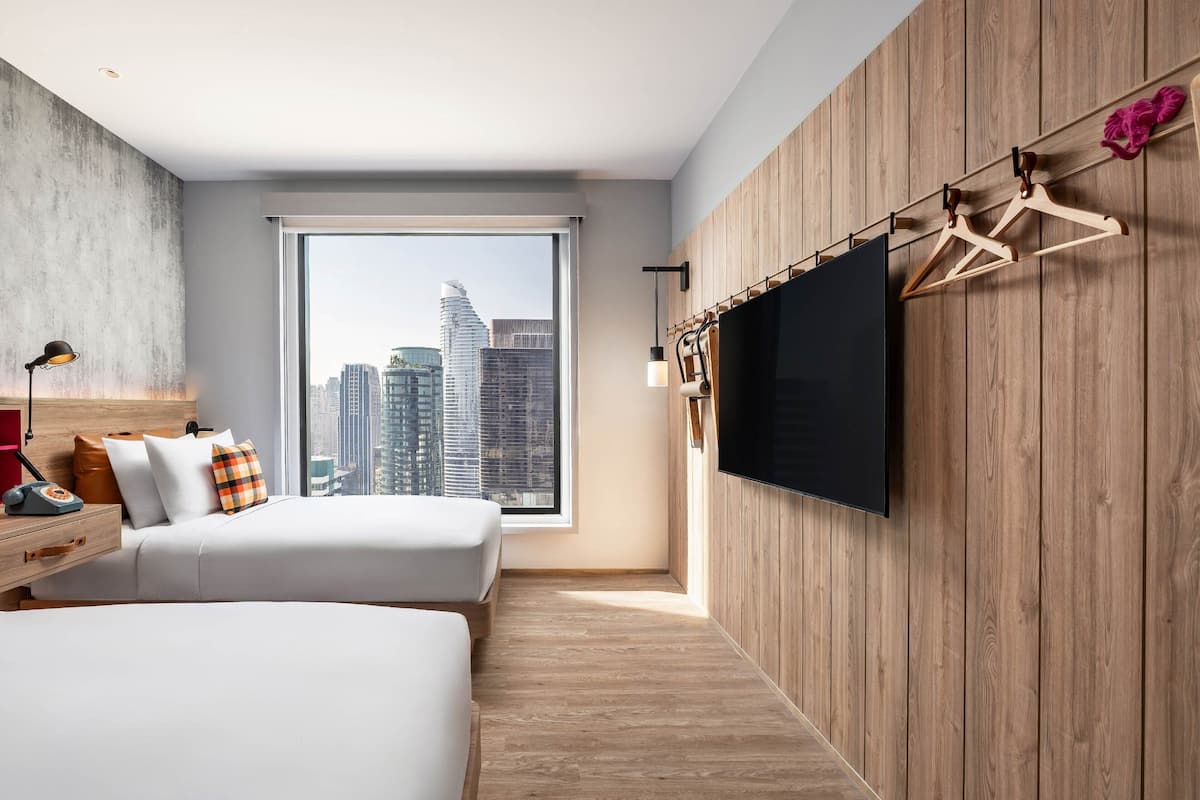 Quarto de hotel moderno com uma janela grande, painéis de madeira, televisão de tela plana e uma cama com roupa de cama branca.
