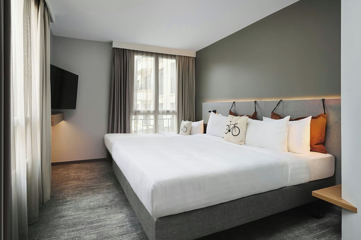 Quarto de hotel com uma cama grande, televisão na parede e janela com cortinas.
