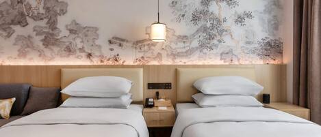 Quarto de hotel com duas camas, uma mesa de cabeceira com abajur e uma parede com pintura tradicional.