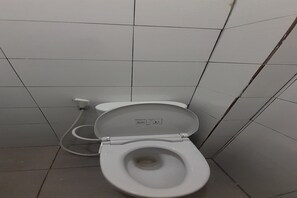 Uma casa de banho pequena e revestida a azulejos, com uma sanita branca e um cano de água visível.