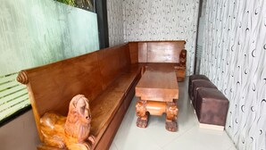 Um sofá de madeira com uma escultura de leão, uma mesa de madeira combinando e um banquinho marrom em um quarto com papel de parede estampado.