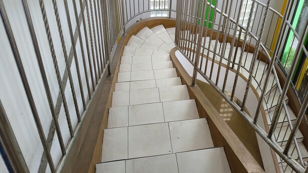 Escada em espiral com guarda-corpos de metal e azulejos brancos.