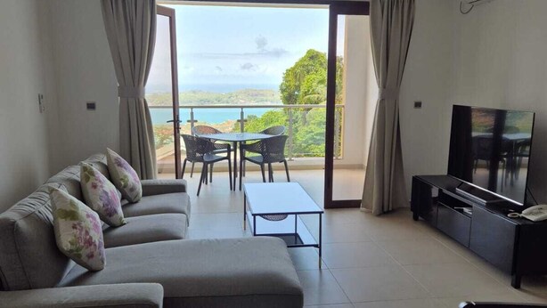Sala de estar moderna com sofá, TV e varanda com vista para o mar.