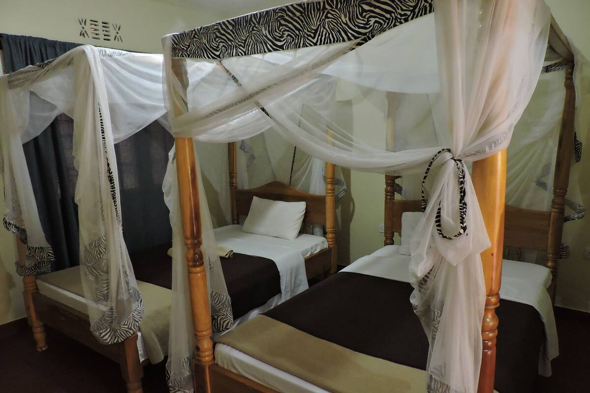 Quarto com três camas de madeira, cada uma com colcha de dossel e saia de cama branca.