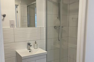 Uma casa de banho moderna com cabine de chuveiro em vidro, lavatório branco com torneira e espelho em cima.