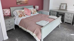Quarto com cama, mesas de cabeceira, penteadeira e um quadro na parede.