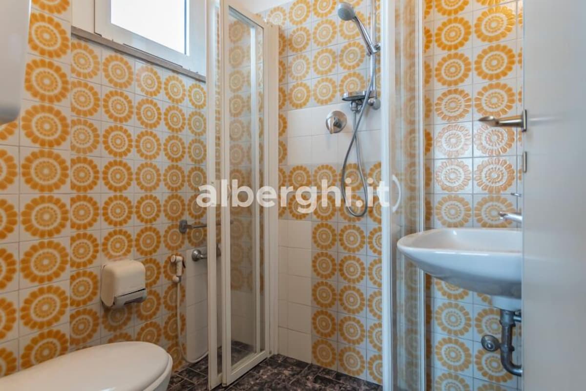 Casa de banho com chuveiro, sanita e lavatório, com design de azulejos estampados.