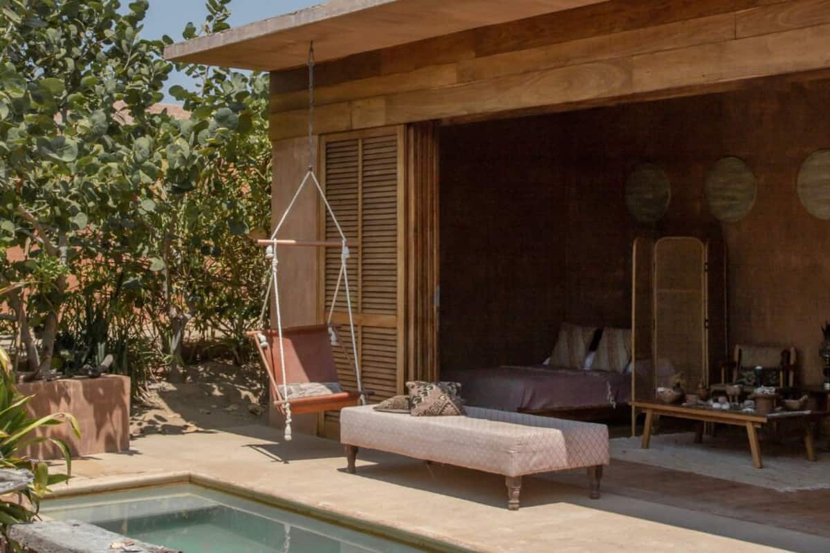 Uma área à beira da piscina com espreguiçadeira, mesa pequena e um banco.