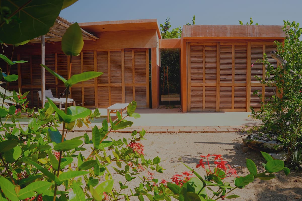 Um edifício moderno com um pátio coberto, área de estar e um jardim com flores vermelhas.
