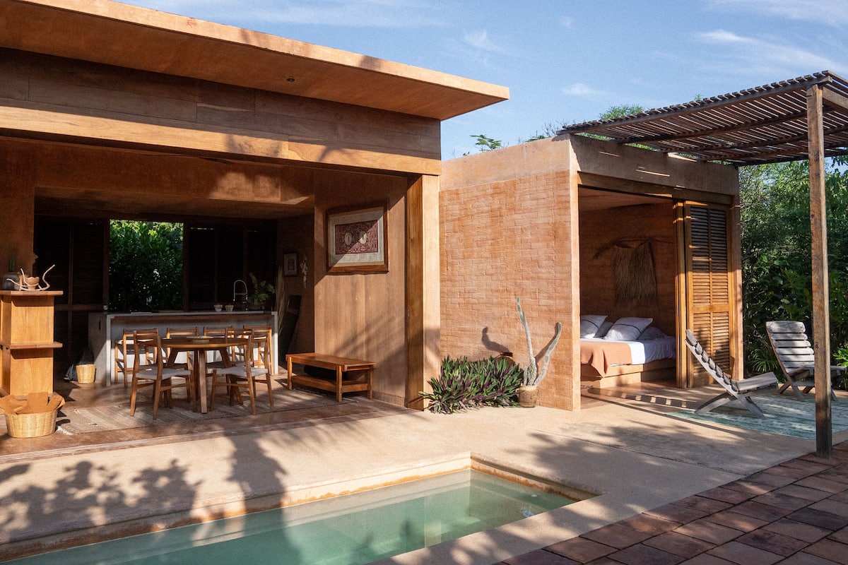 Uma área moderna com piscina ao ar livre, deck de madeira, espreguiçadeiras e espaço de refeições com mesas e cadeiras.