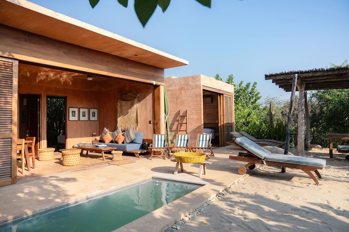 Uma área de piscina moderna ao ar livre, com espreguiçadeiras, um deck de madeira e um espaço de estar coberto.