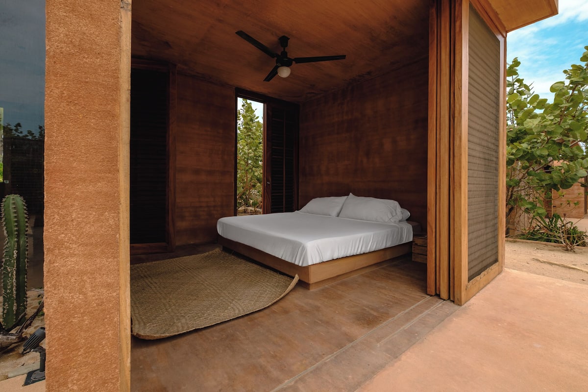Quarto com cama, ventilador de teto e vista para o exterior.