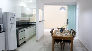 Cozinha compacta com eletrodomésticos brancos, uma mesa de jantar com cadeiras e uma luminária pendente.
