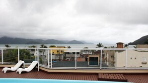 Área de piscina com espreguiçadeiras e vista para o mar e montanhas.