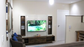 Sala de estar com televisão de tela plana na parede, uma unidade de entretenimento de madeira embaixo e uma porta à direita.