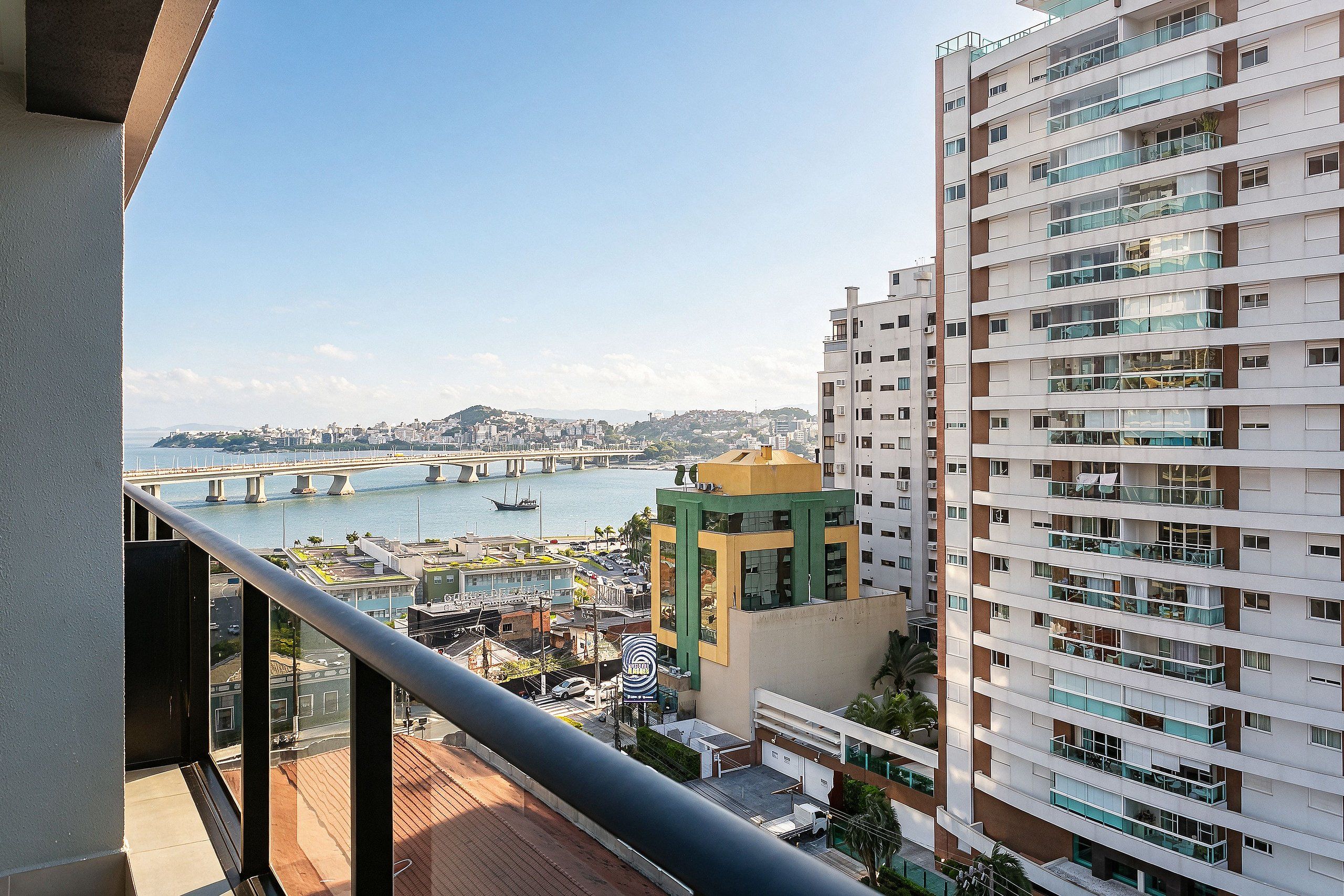 Um edifício alto com várias varandas a dar para um porto e uma ponte.