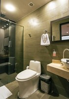 Uma casa de banho moderna com cabine de duche em vidro, sanita branca, lavatório com bancada de mármore e espelho sobre o lavatório.