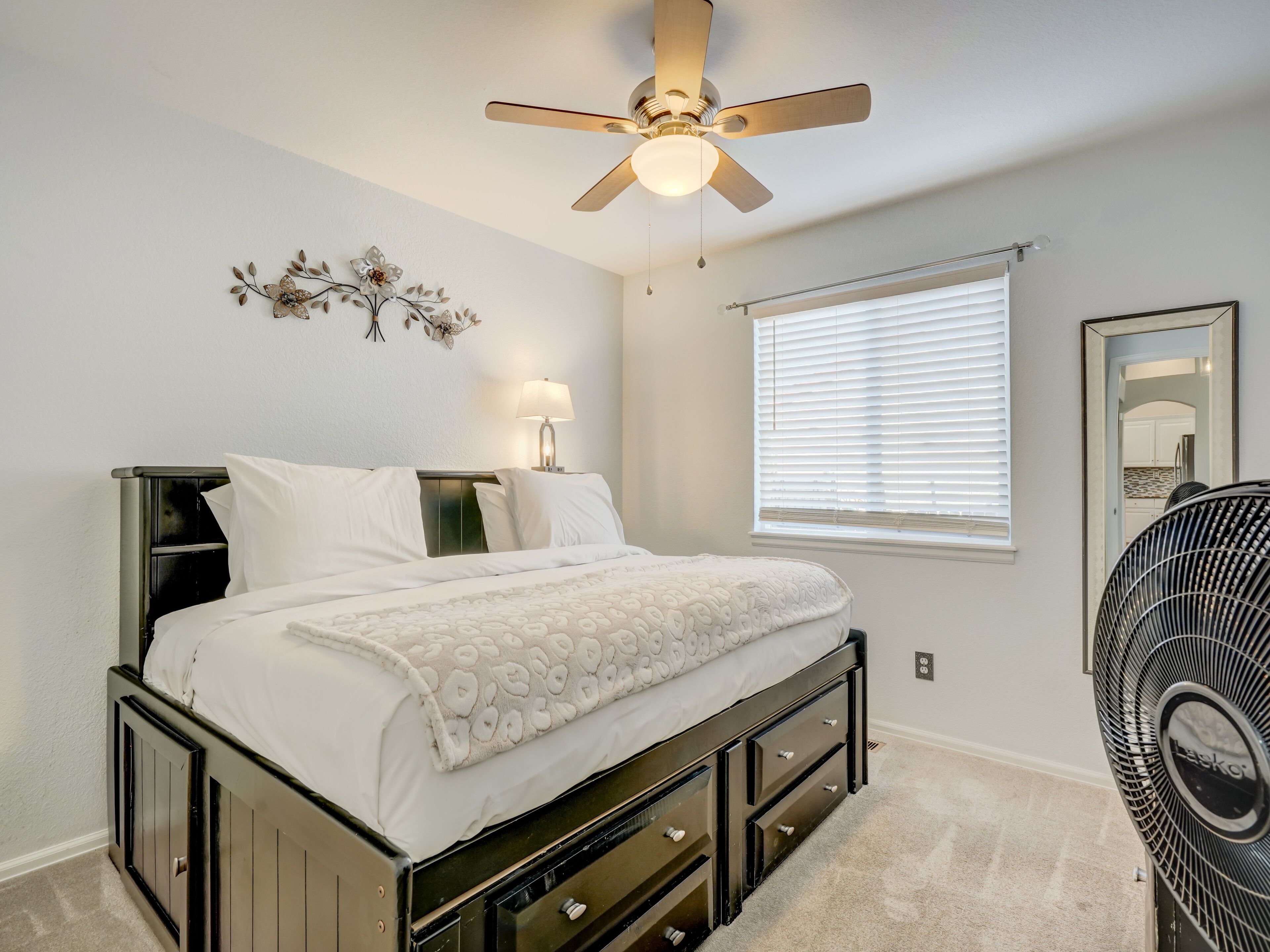 Quarto com cama, ventilador de teto, luminária na parede, janela com persianas e espelho.