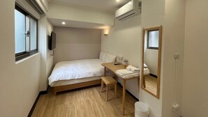 Quarto de hotel pequeno com uma cama, mesa de cabeceira com abajur, espelho e janela.