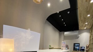 Uma área de recepção com balcão branco, um letreiro iluminado grande e painel de parede de madeira.