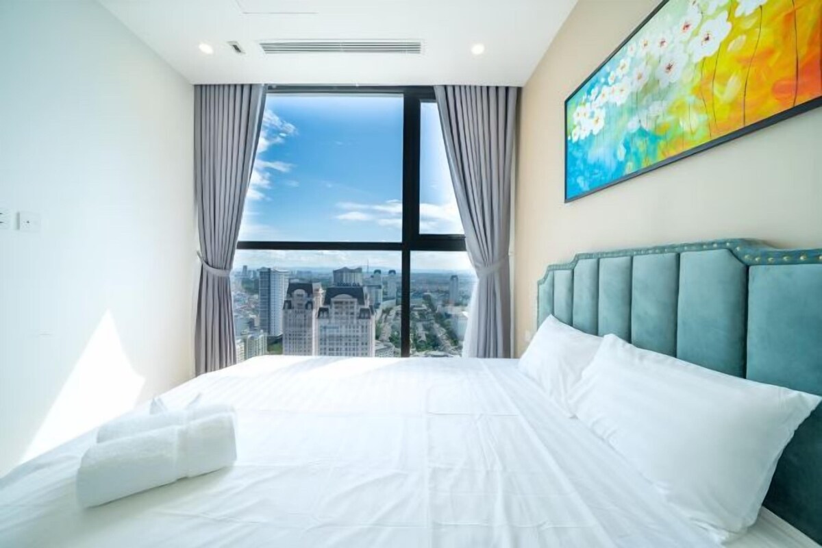 Quarto de hotel com uma cama grande, vista para a cidade e uma pintura colorida na parede.